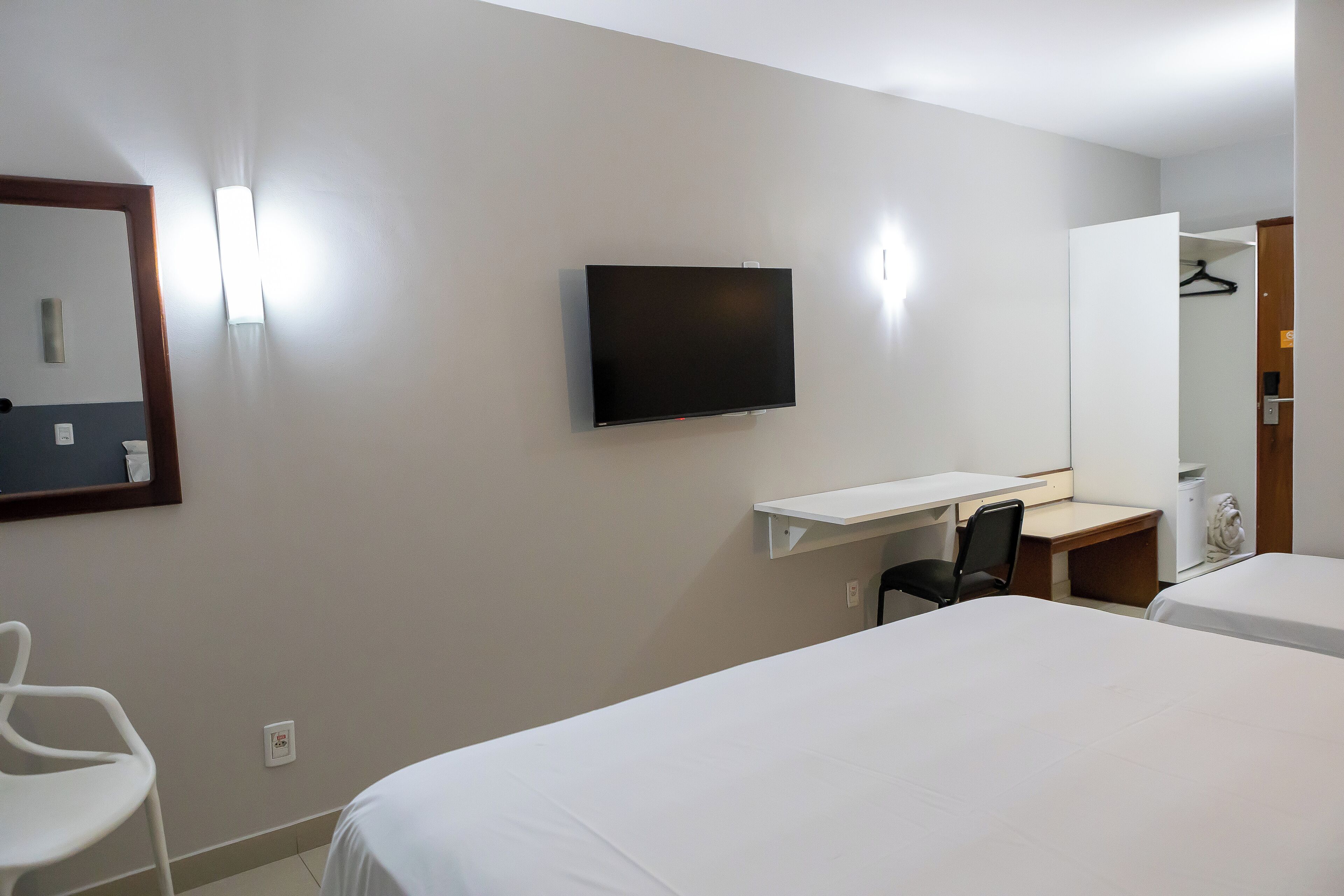 Quarto de hotel com cama, escrivaninha, cadeira, televisão e armário.