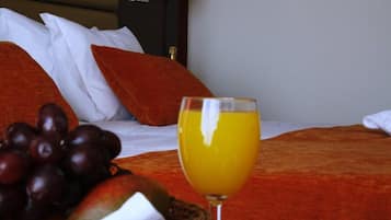 Uma cama com roupa de cama branca e laranja, um copo de suco de laranja e uma cesta de frutas.