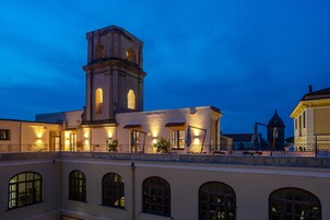Edifício histórico com uma torre imponente e janelas em arco, apresentando área de estar ao ar livre e varanda com grades.