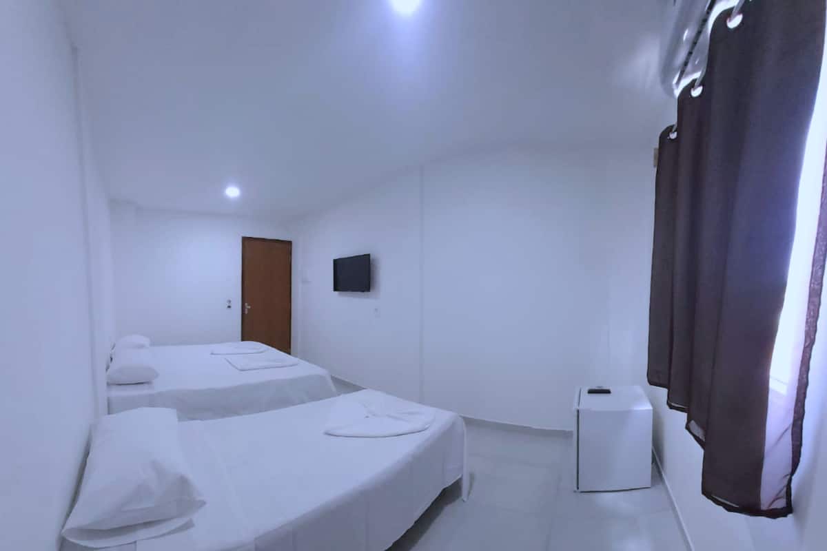 Quarto com duas camas, uma televisão pequena, uma porta e uma janela com cortinas.