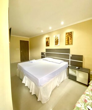 Quarto moderno com uma cama grande, uma mesinha de cabeceira e um painel de cabeceira.