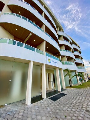 Um hotel de vários andares com fachada curva, uma palmeira e uma placa com o texto 'Beira Mar Hotel'.
