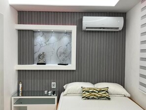 Quarto moderno com cama, mesa de cabeceira e ar condicionado.