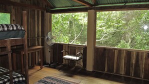 Quarto de madeira com uma cama beliche, uma cadeira e um ventilador.