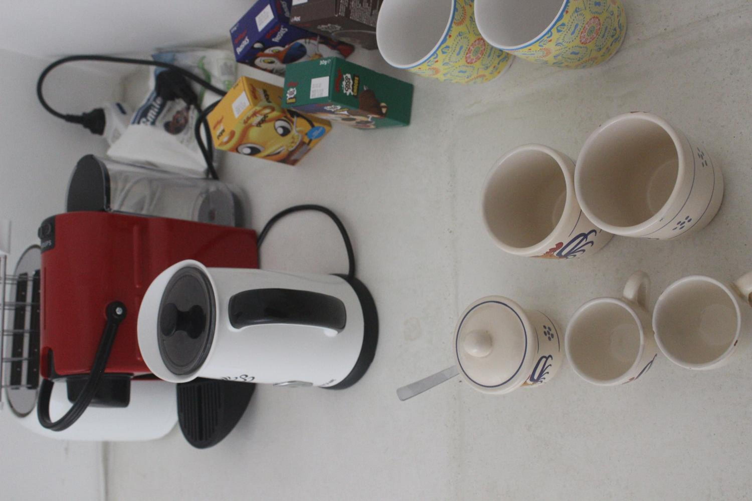 Uma área de cozinha com um eletrodoméstico vermelho, possivelmente uma cafeteira, e vários copos brancos com desenhos azuis.