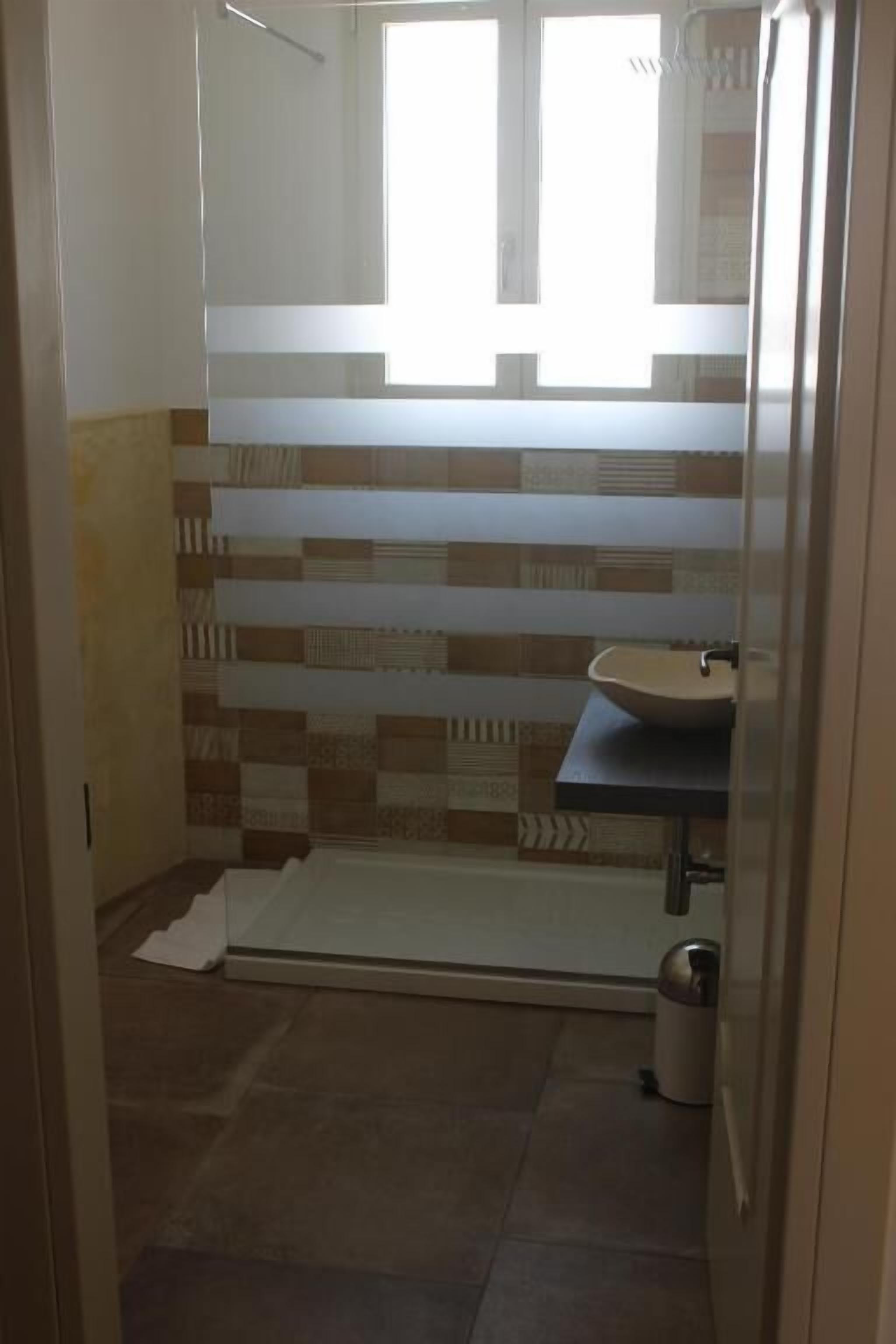 Casa de banho com painel de azulejos estampados, uma pia e um cesto de lixo.