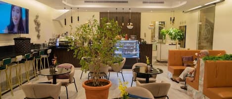 Um saguão de hotel moderno com área de bar, espaços para sentar e uma tela de televisão.