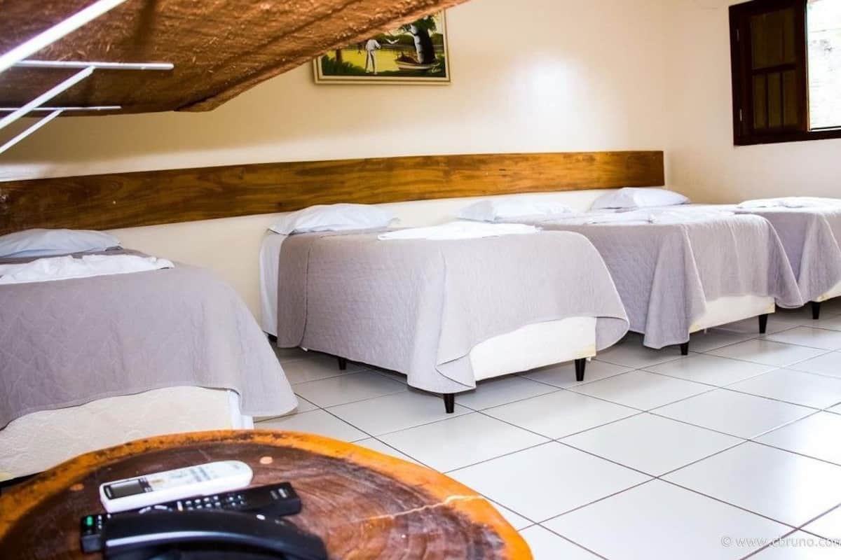 Quarto de hotel com quatro camas de solteiro, cabeceira de madeira, piso de azulejos e um controle remoto sobre uma mesa de madeira.
