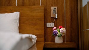 Uma cama bem arrumada com cabeceira de madeira, mesa de cabeceira com tomada e um vaso de flores.