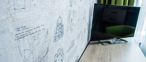 Uma mesa com monitor de computador, um caderno com esboços arquitetônicos e uma cortina verde.