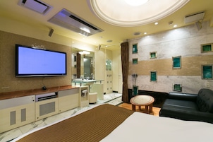 Quarto de hotel com televisão, sofá, cama e banheiro com espelho e pia.