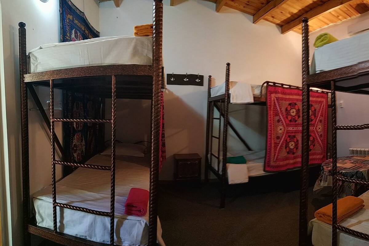 Quarto de dormitório com três beliches, uma mesinha e uma prateleira fixada na parede.