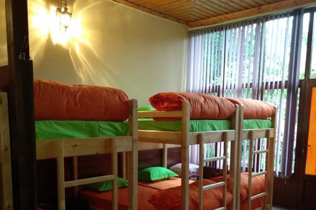 Quarto com beliches, teto de madeira e janela com cortinas.