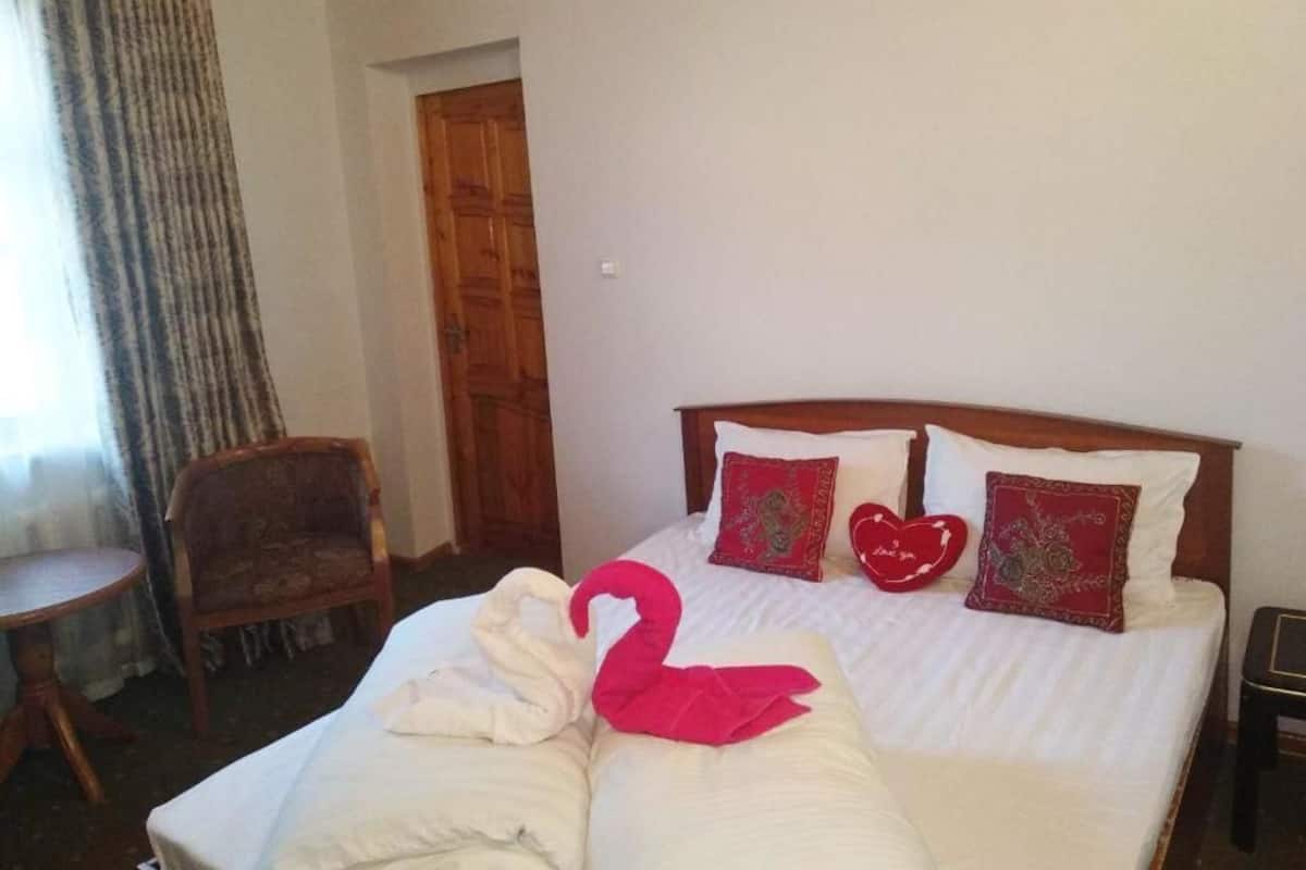 Quarto de hotel com uma cama, duas almofadas, uma cadeira e uma pequena mesa.