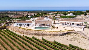 Uma propriedade costeira com piscina, fileiras de vinhas e um edifício branco com telhado em azulejos.