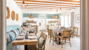 Uma sala de jantar com mesas e cadeiras de madeira, um sofá azul e luminárias pendentes.