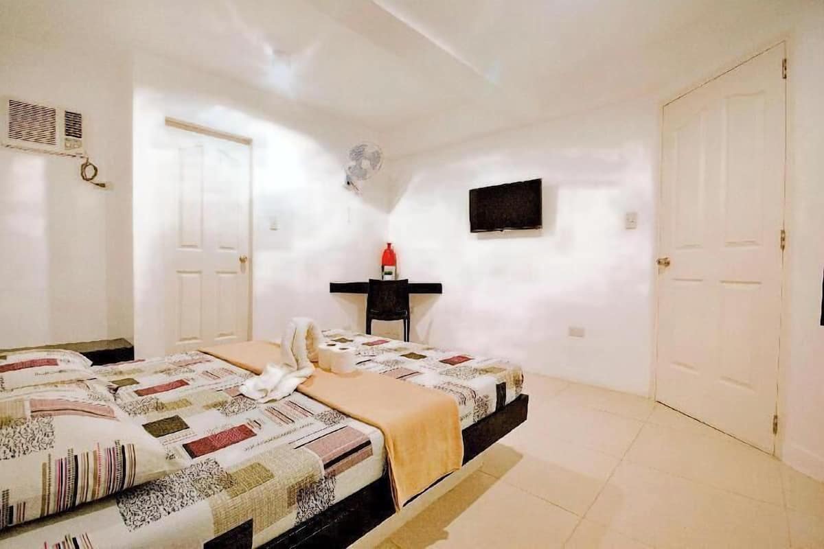 Quarto com duas camas, uma televisão na parede, aquecedor e porta.