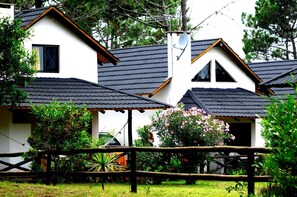 Uma fileira de casas brancas com telhados escuros, cercada por vegetação e um portão de madeira.
