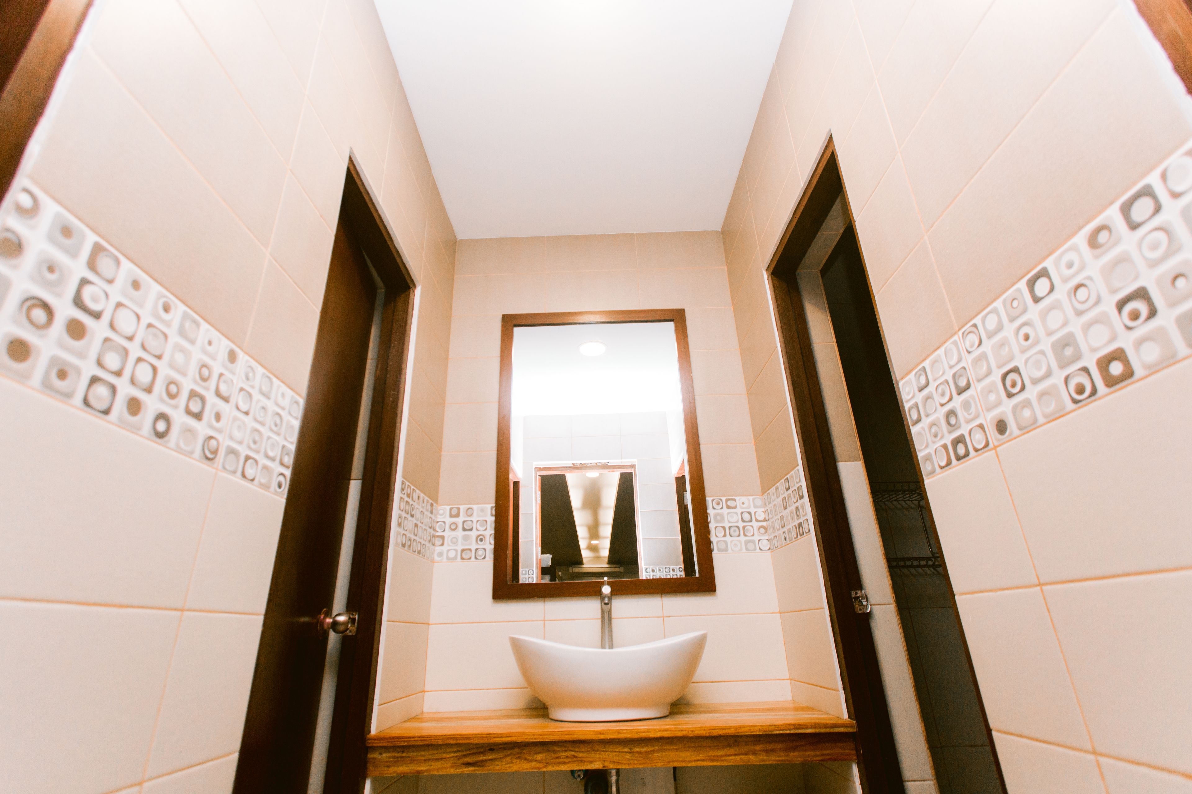 Um banheiro com pia branca, espelho e azulejos estampados nas paredes.