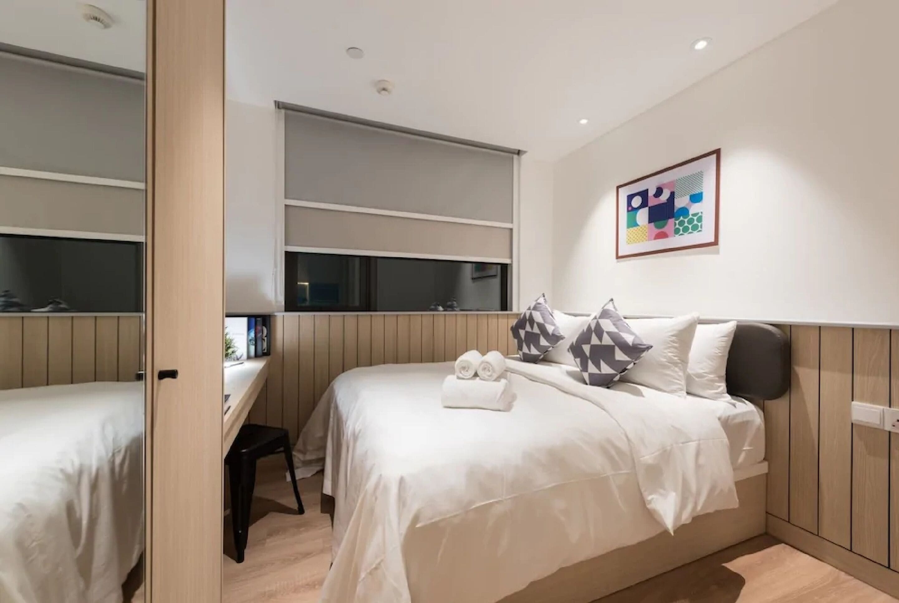 Quarto com cama, escrivaninha e prateleira na parede.