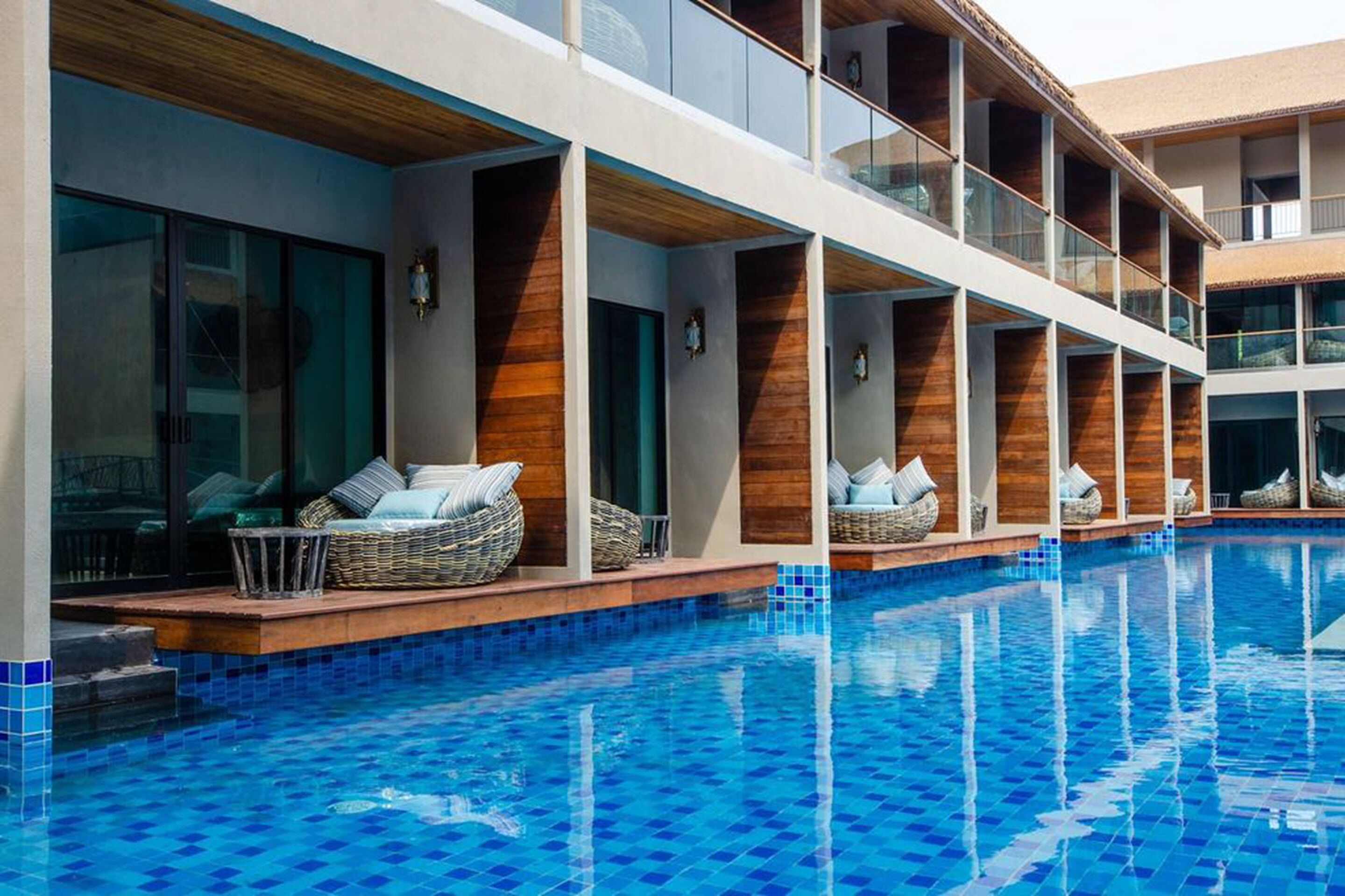 Um hotel moderno com piscina, área de estar externa com móveis de vime e estrutura em vários andares.