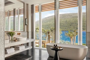 Um banheiro moderno com uma banheira de pedestal, um espelho grande, uma pia e vista para uma paisagem montanhosa através de grandes janelas.