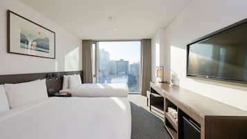 Quarto de hotel com duas camas, uma escrivaninha, televisão e uma janela grande com vista para a cidade.