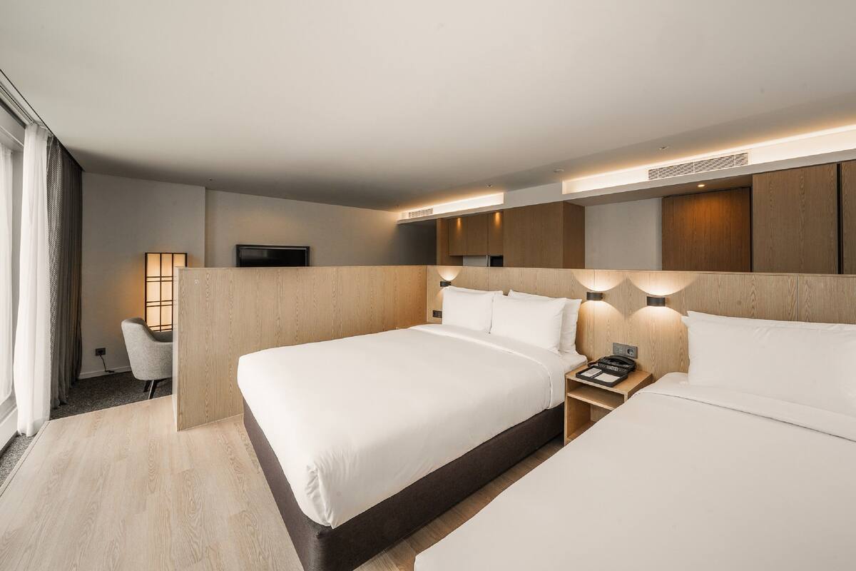 Quarto de hotel moderno com duas camas, uma escrivaninha e uma televisão.