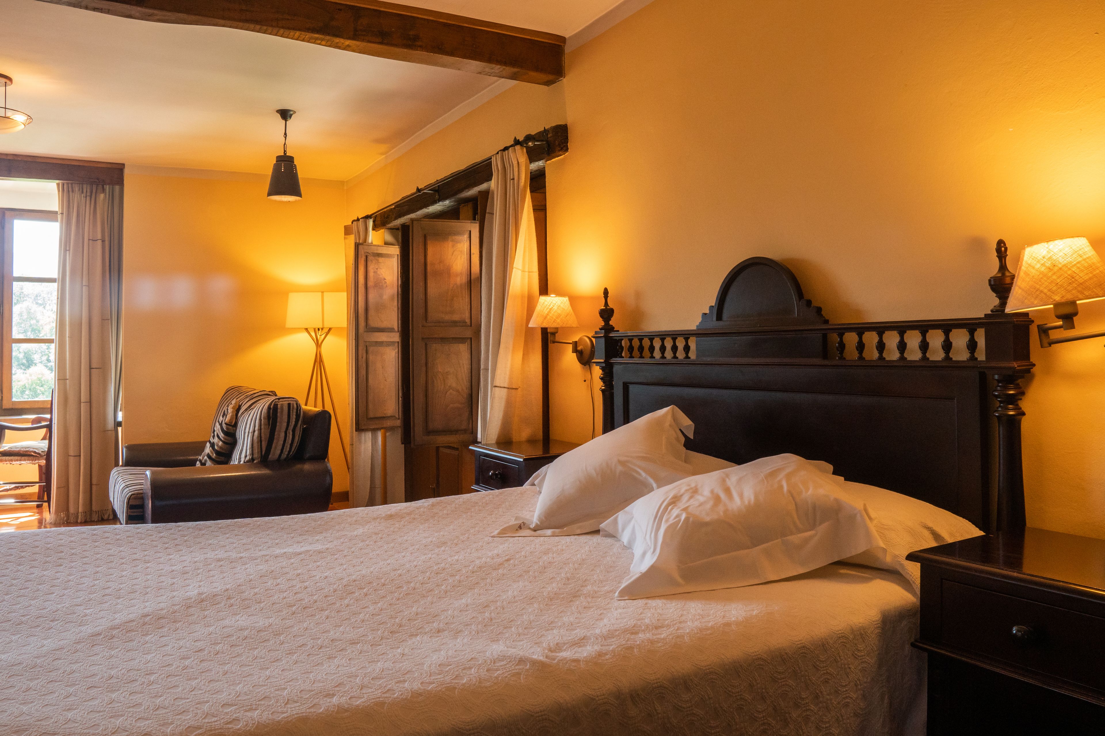 Cama bem arrumada com lençóis brancos, cabeceira de madeira e duas luminárias de cabeceira.