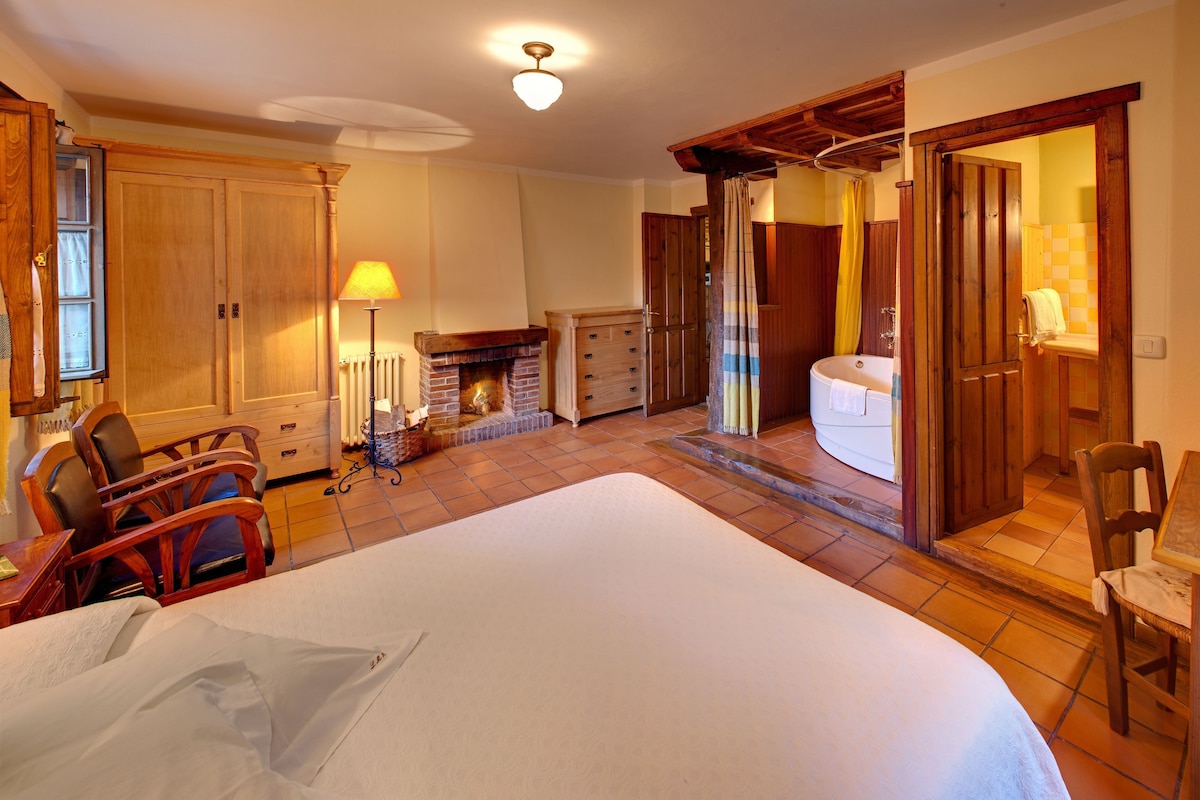 Quarto espaçoso com cama grande, móveis de madeira, lareira e banheiro com banheira.