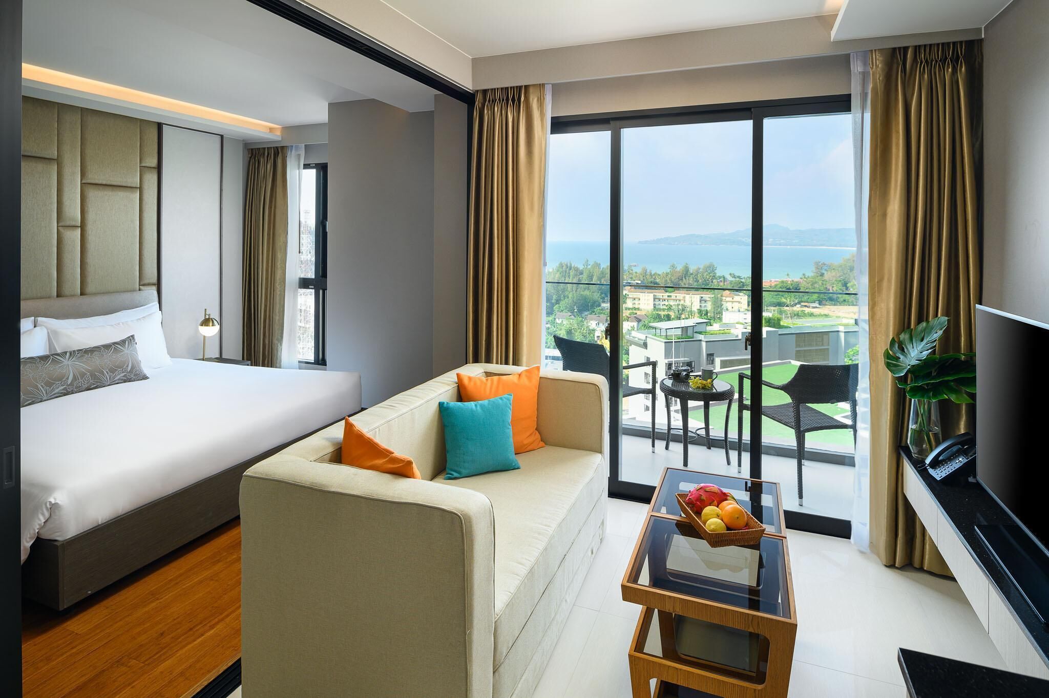 Quarto de hotel moderno com cama, sofá e área de jantar com mesa e cadeiras.