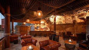 Um espaço de bar acolhedor com assentos de couro, mesas de madeira e uma parede de pedra rústica.
