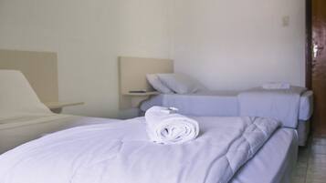 Quarto de hotel com duas camas, cada uma com almofada e uma toalha enrolada.
