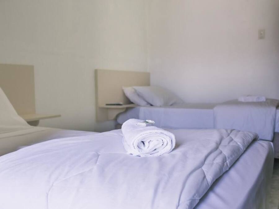 Quarto de hotel com duas camas, cada uma com almofada e uma toalha enrolada.