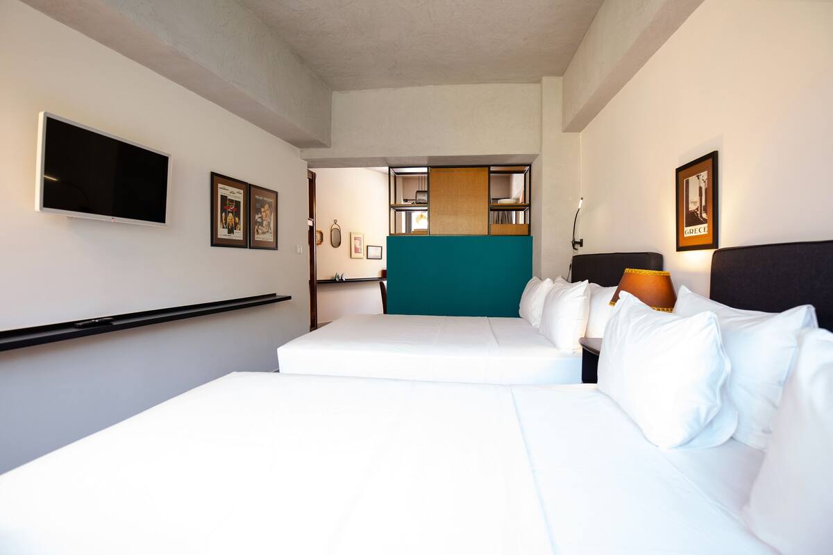 Quarto de hotel com uma cama grande, televisão e uma pequena escrivaninha.