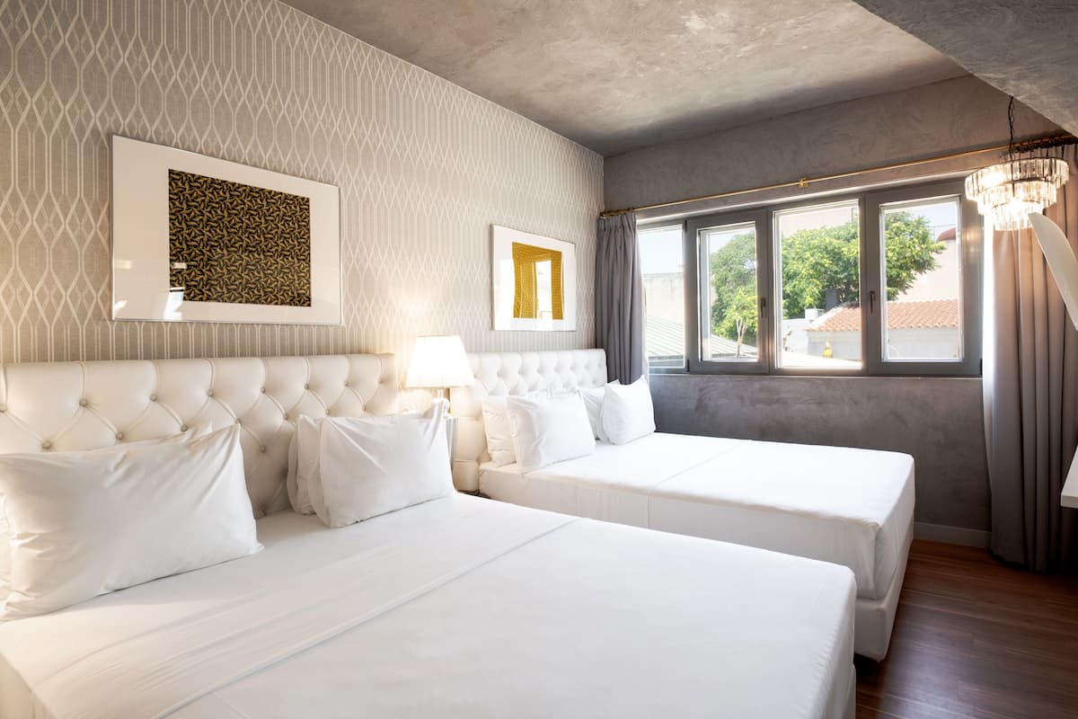 Quarto de hotel com uma cama grande, duas camas menores, um lustre e uma janela com vista para o exterior.