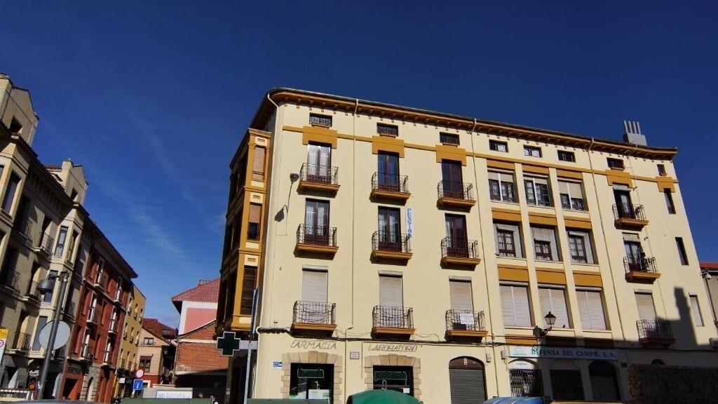 Um edifício de vários andares com fachada amarela, várias varandas e lojas no andar térreo.