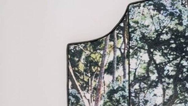 Quarto com uma cama, um abajur de chão preto e uma parede com estampa de floresta.