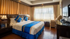 Quarto de hotel com uma cama grande, uma escrivaninha, uma cadeira e uma televisão.