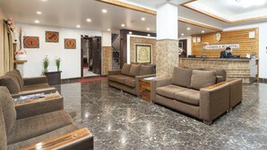Um saguão de hotel com balcão de recepção, sofás e piso de mármore.