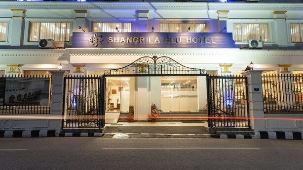 Exterior do Hotel Shangrila Blu, com um portão de entrada imponente e unidades de ar condicionado na fachada.