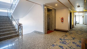 Um hall de hotel com uma escadaria de granito, um elevador de mármore e um tapete estampado.