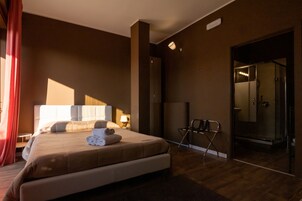 Quarto de hotel moderno com uma cama grande, área de estar e chuveiro em cabine de vidro.