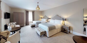 Quarto de hotel com duas camas, área de estar com mesa e cadeiras, um espelho grande e um lustre.