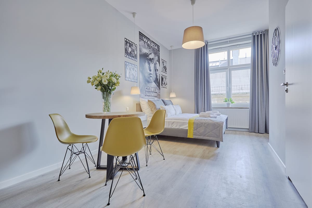 Quarto moderno com cama, mesa de jantar com cadeiras, janela com cortinas e parede com quadros.