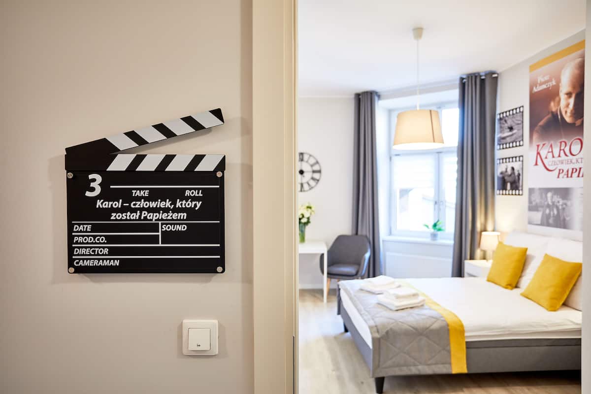 Quarto de hotel com uma cama, uma escrivaninha e um claquete fixado na parede.