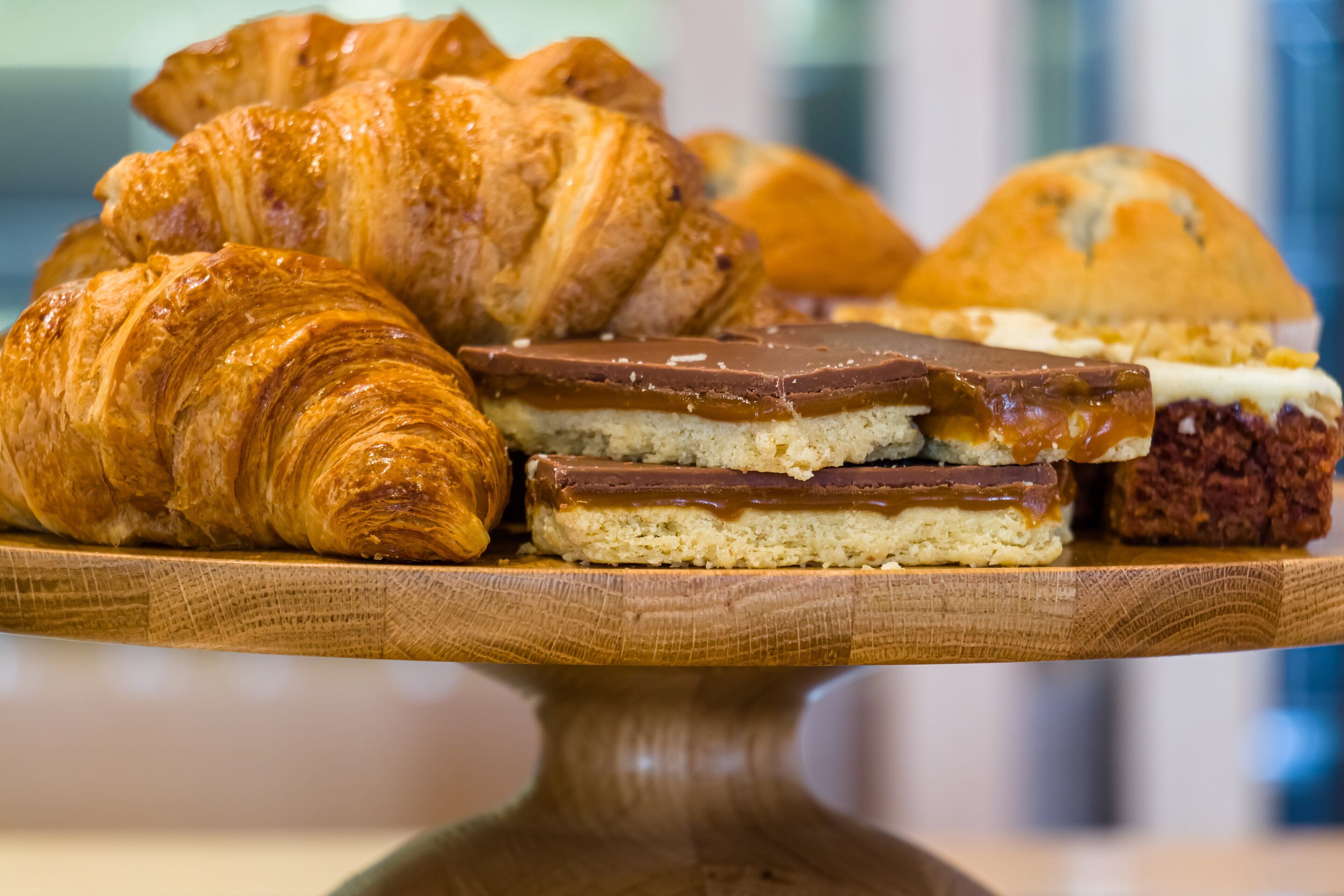 Uma tábua de madeira com diversos doces, incluindo croissants e uma sobremesa em camadas.