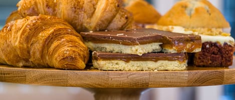 Uma tábua de madeira com diversos doces, incluindo croissants e uma sobremesa em camadas.