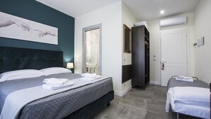 Quarto de hotel com uma cama grande, uma cama menor, um guarda-roupa, banheiro com espelho e unidade de ar condicionado.