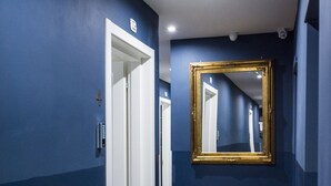 Um corredor com paredes azul escuro, chão ladrilhado e um espelho grande na parede.